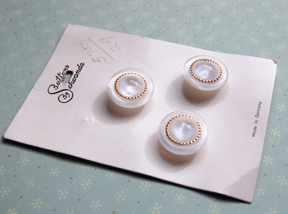 Brett med hvitblanke knapper med gullring. - Epla